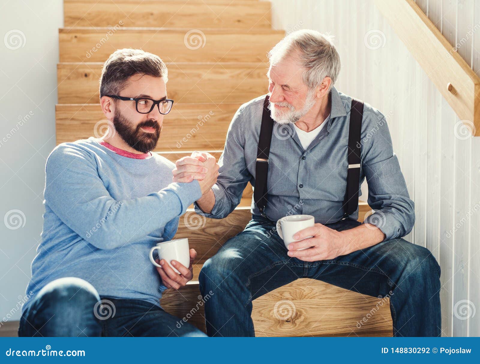 An Adult Hipster Son And Senior Father Sitting On Stairs Indoors At