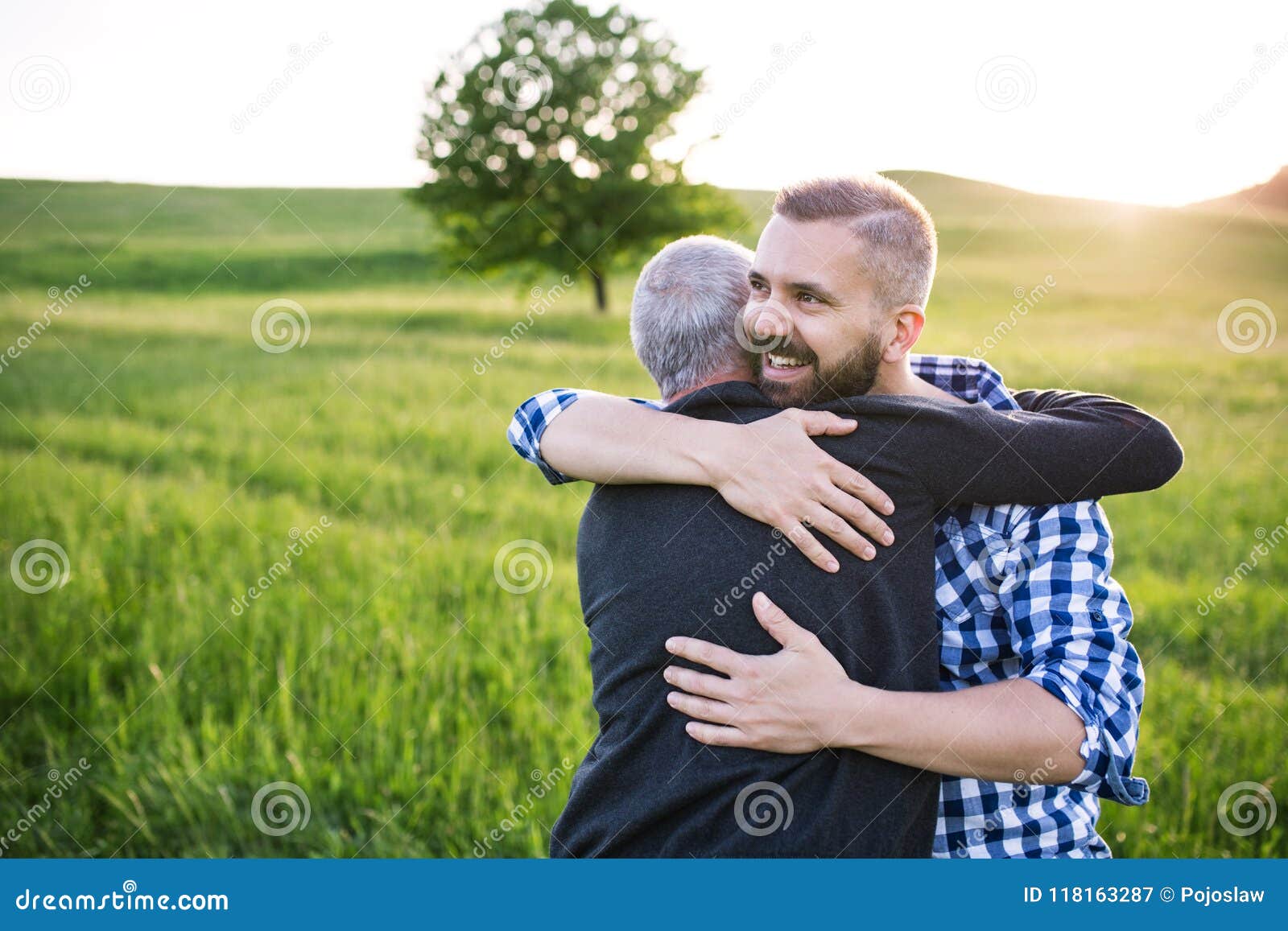 An Adult Hipster Son With Senior Father On A Walk In Nature At Sunset