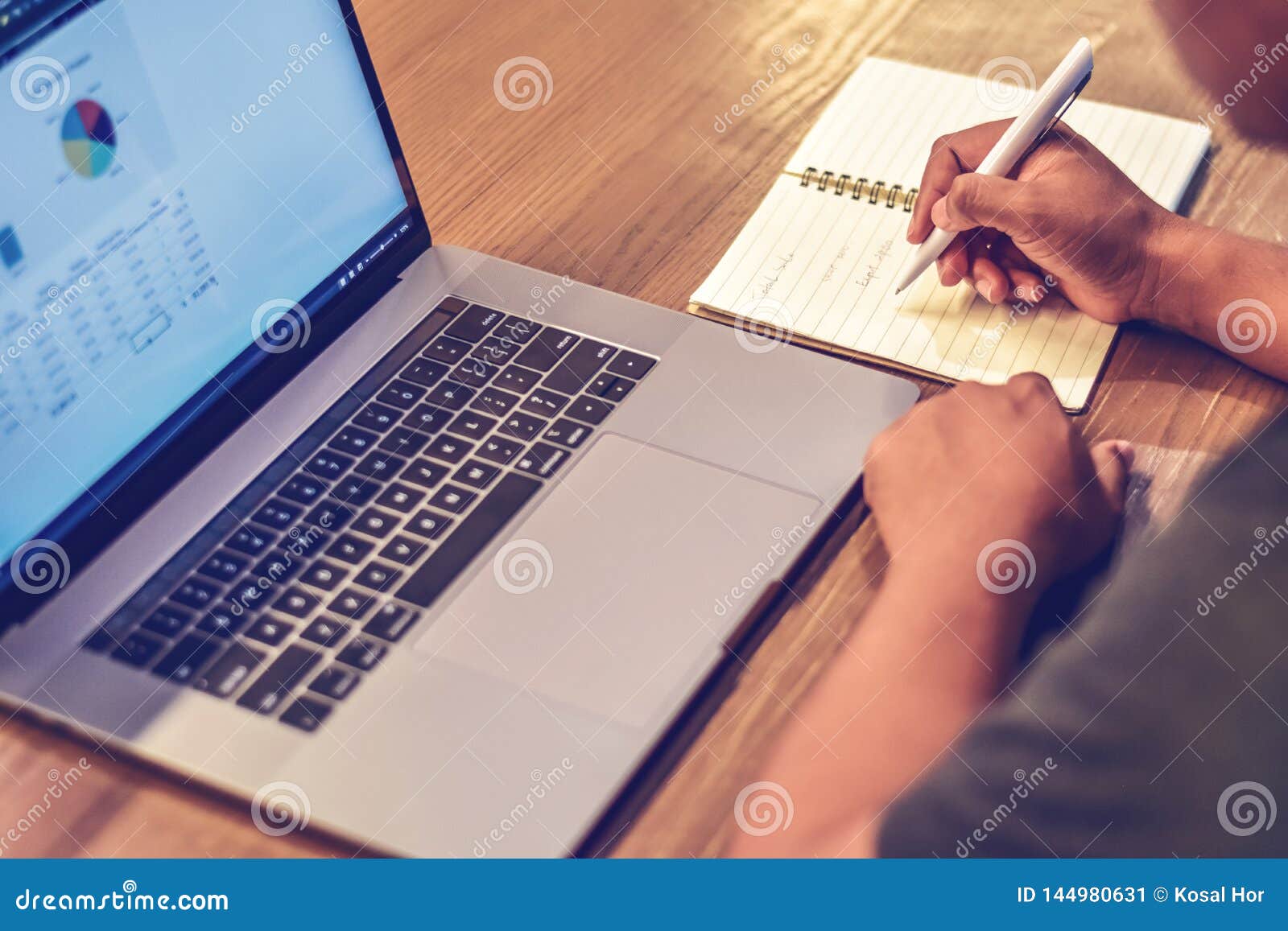 Adult Man Writing Note on a Notebook beside Laptop on a Desk in Office ...