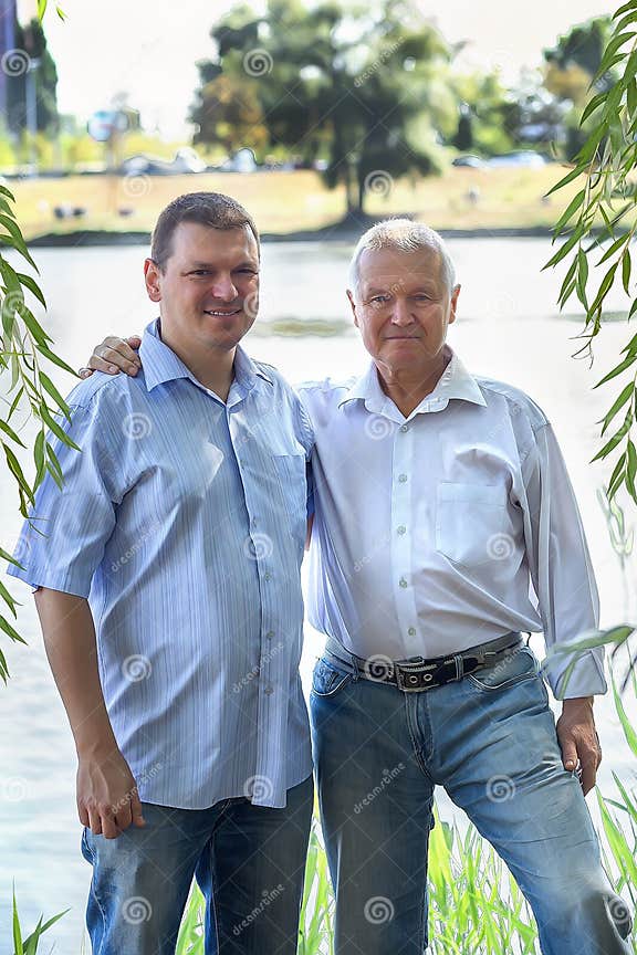 Adult Son And Elderly Father In Blue Shirts And Jeans Standing By The