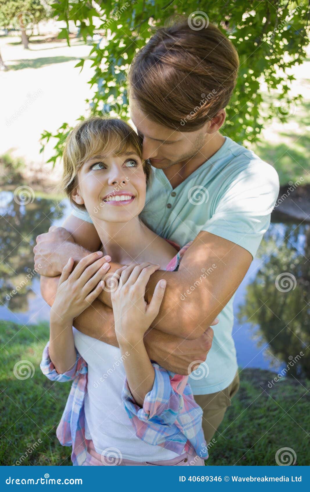 Affectionate Young Couple Standing Together In The Park Smiling At Each