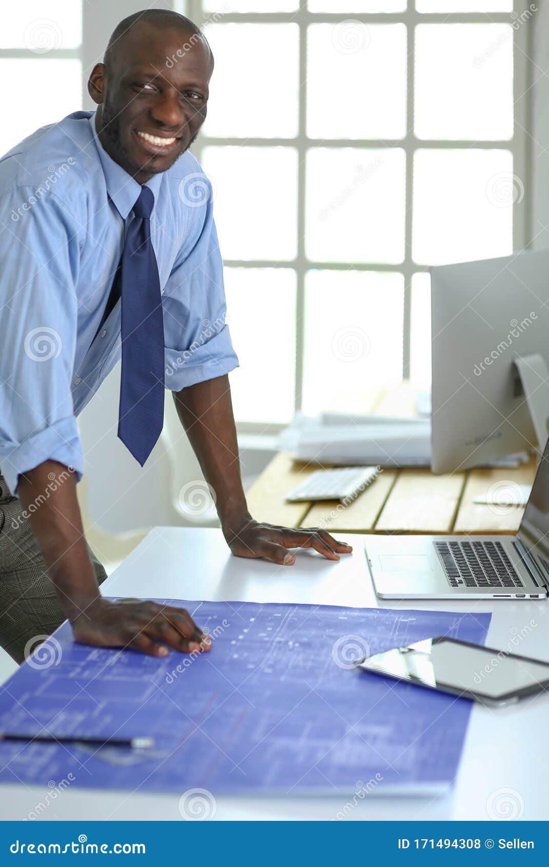 African American Architect Working with Computer and Blueprints in ...