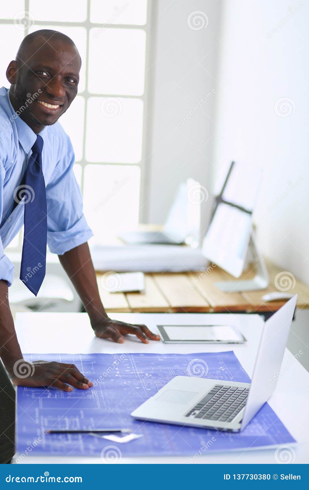 African American Architect Working with Computer and Blueprints in ...