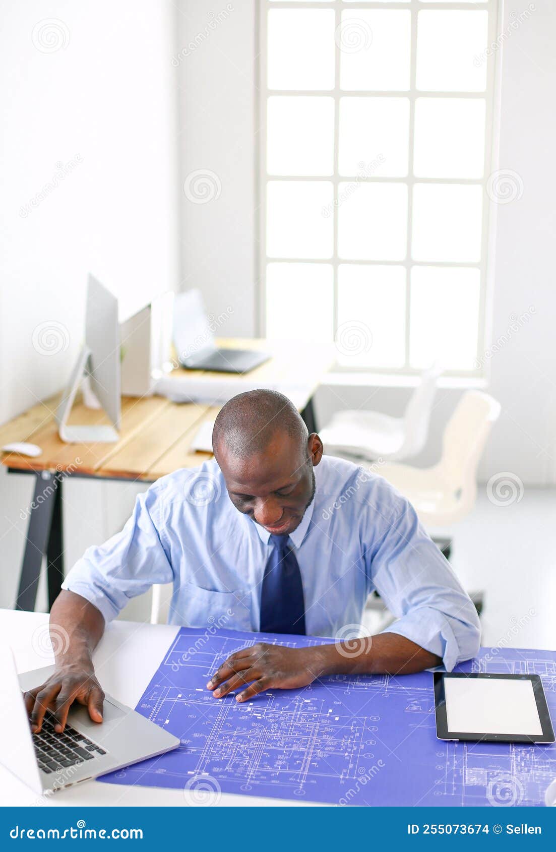 African American Architect Working with Computer and Blueprints in ...