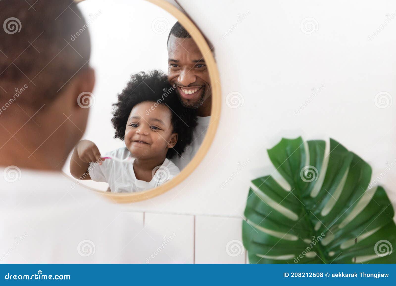 African American Father And Son Looking At Mirror Brushing Teeth In