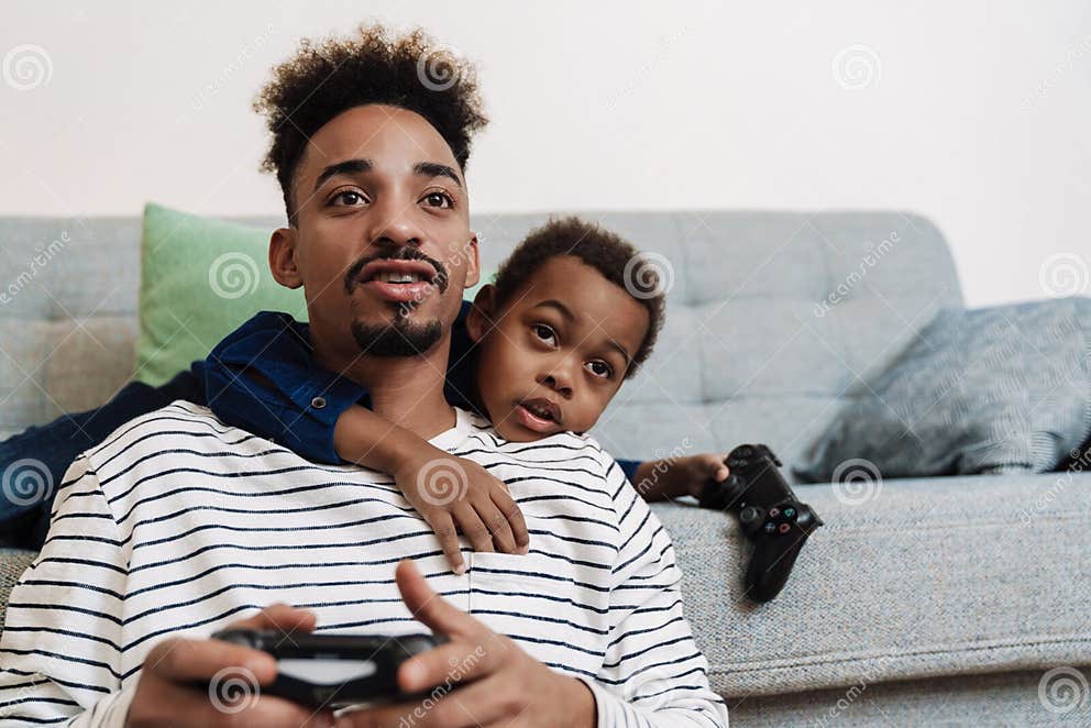 African American Father And Son Playing Video Game While Sitting On