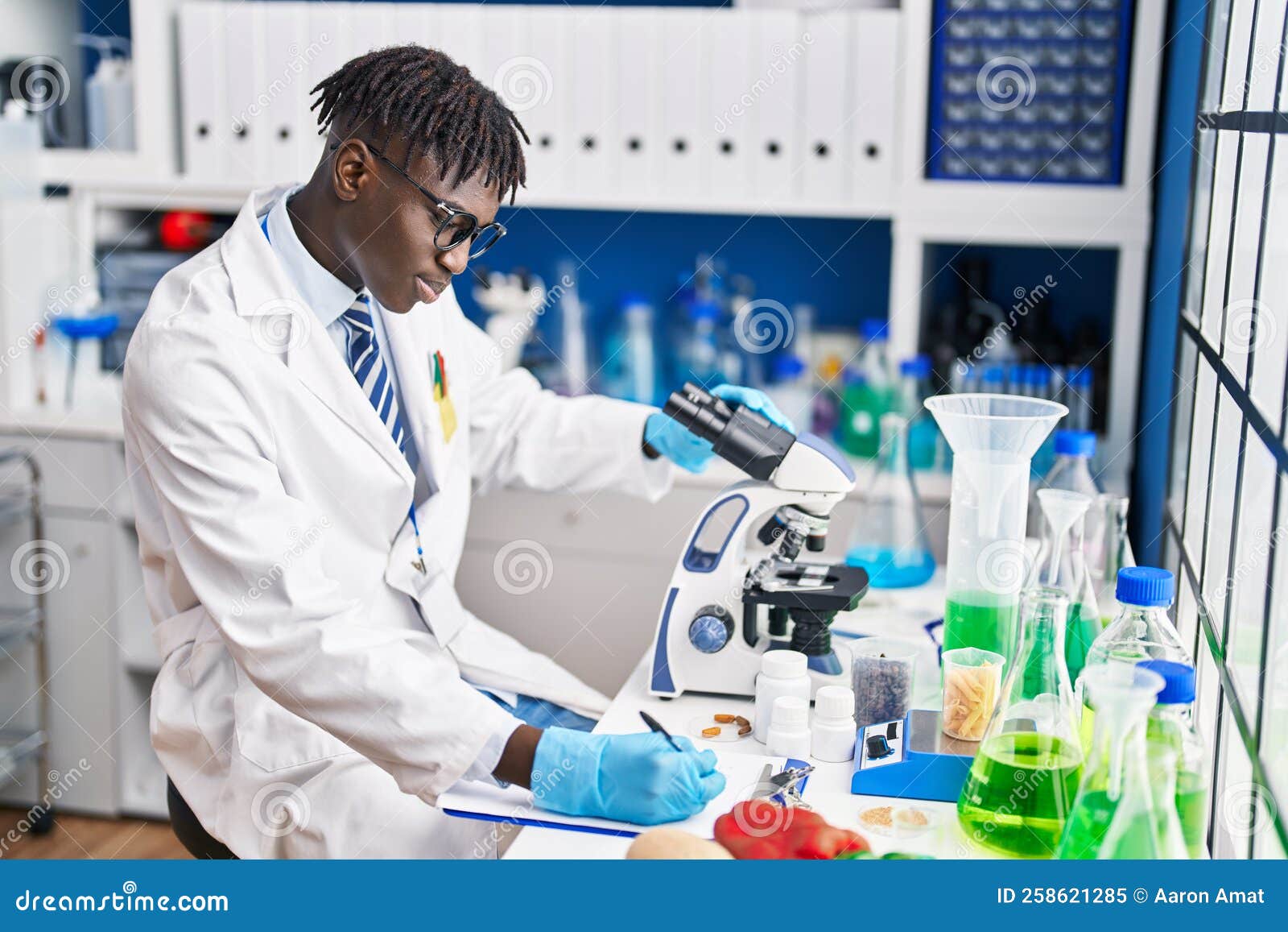 African American Man Scientist Using Microscope Writing Report at ...