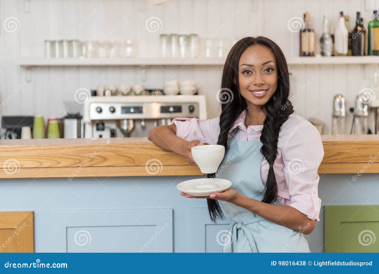 African American Waitress in Apron Drinking Coffee and Looking at ...