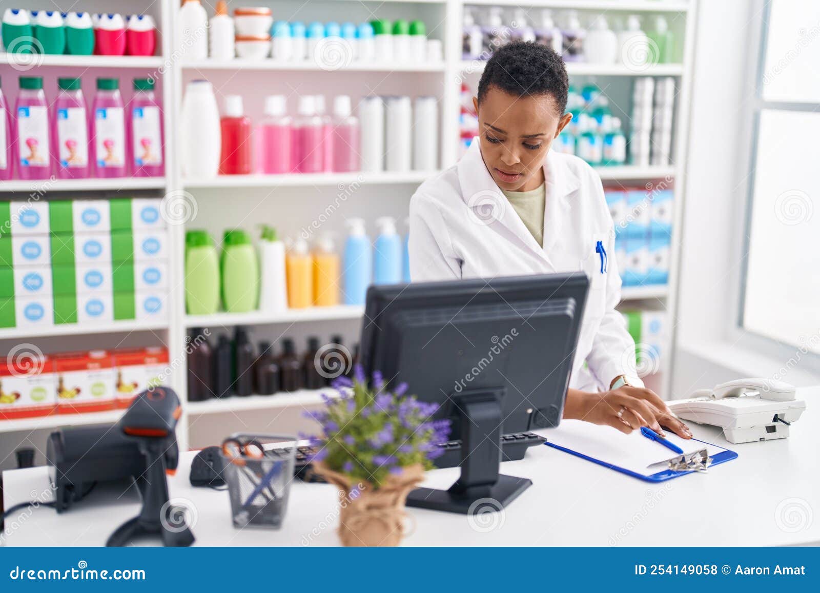 African American Woman Pharmacist Writing on Document Using Computer at ...