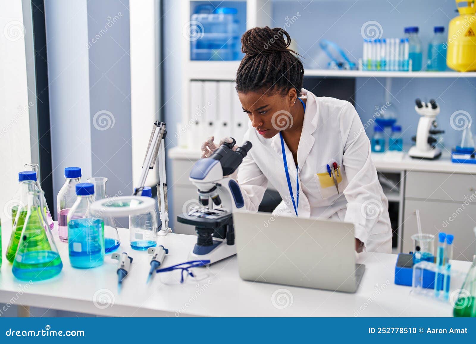 African American Woman Scientist Using Laptop and Microscope at ...