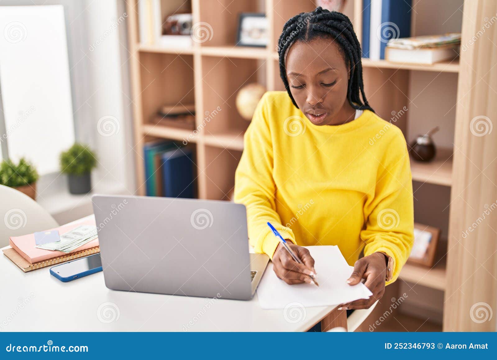 African American Woman Using Laptop Writing on Document at Home Stock ...