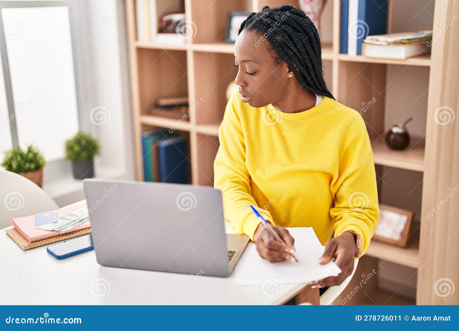 African American Woman Using Laptop Writing on Document at Home Stock ...