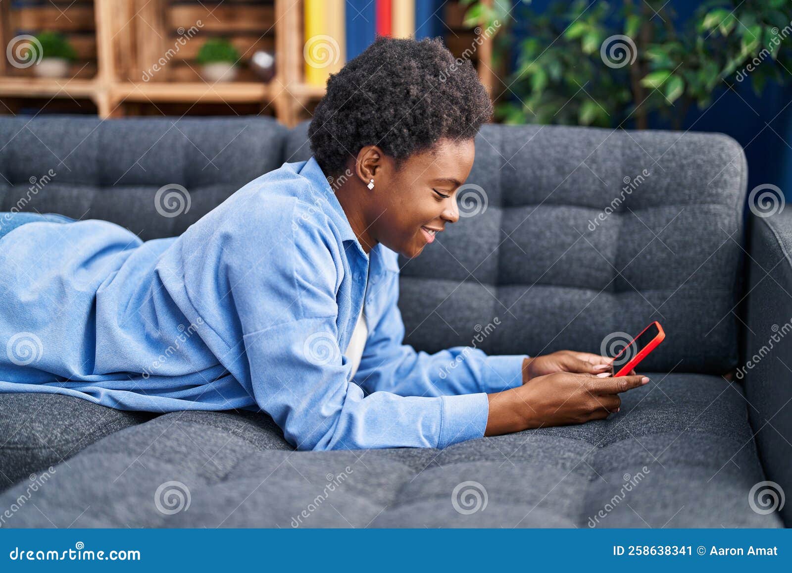 African American Woman Using Smartphone Lying on Sofa at Home Stock ...