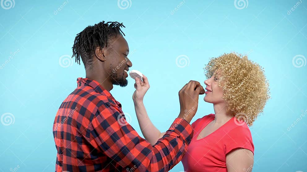 African Man Caucasian Woman Eating Black And White Marshmallows Blue
