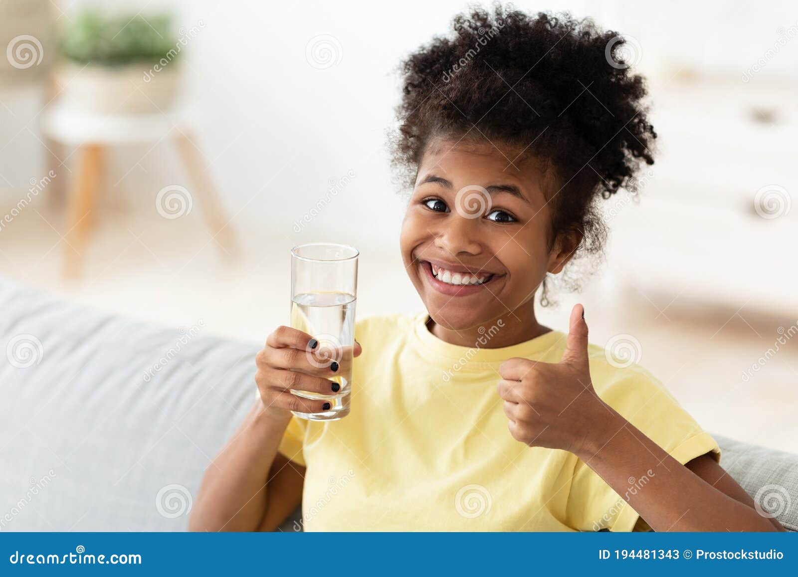 African Teen Girl Holding Glass Of Water Gesturing Thumbs Up Indoor