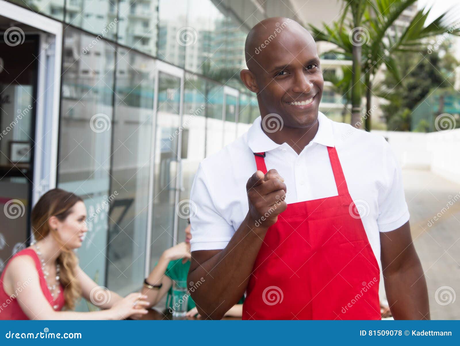 African Waiter at Work in a Restaurant Pointing at Camera with Guests ...
