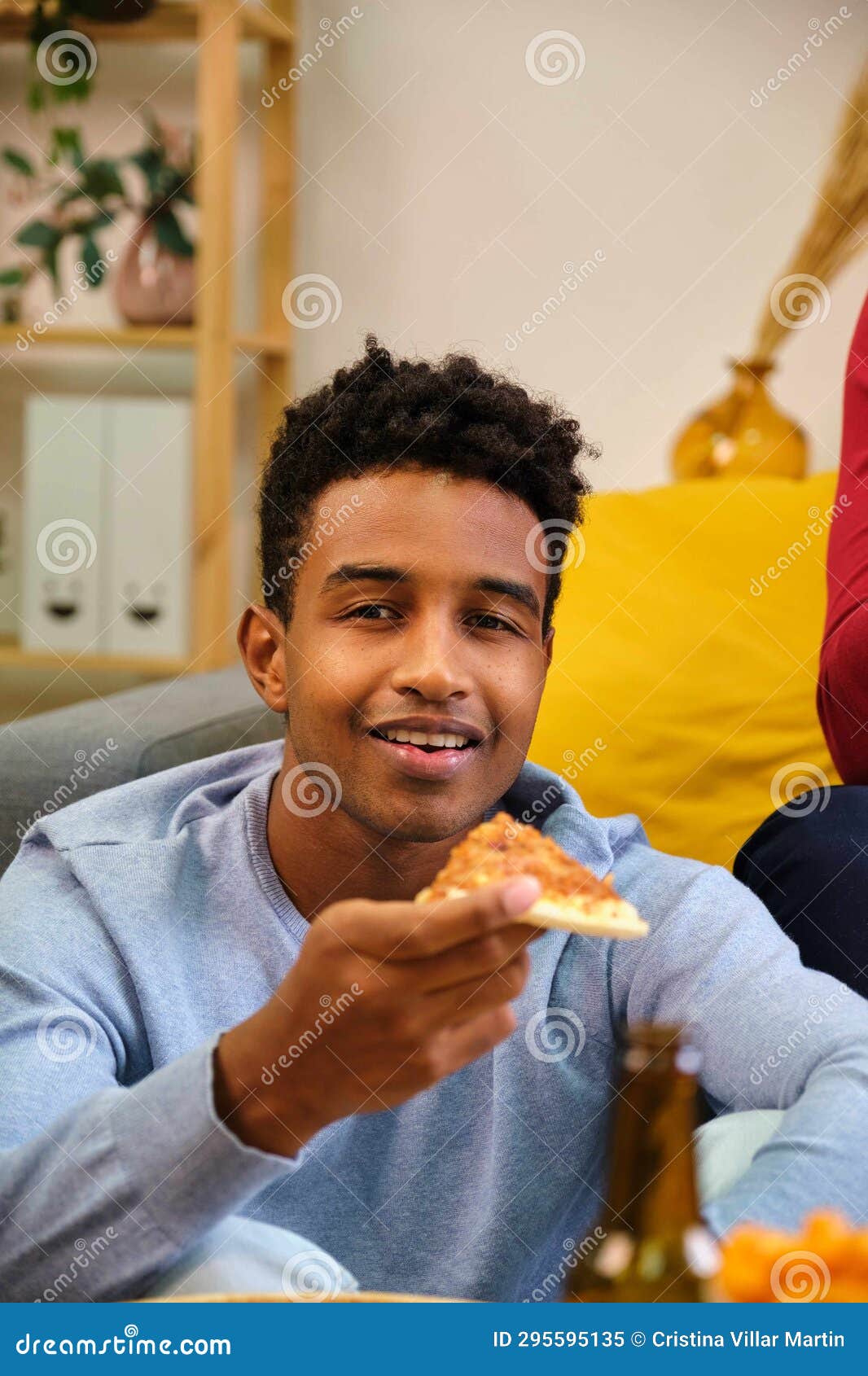 African Young Man Eating Pizza, Smiling and Looking at Camera at Home ...