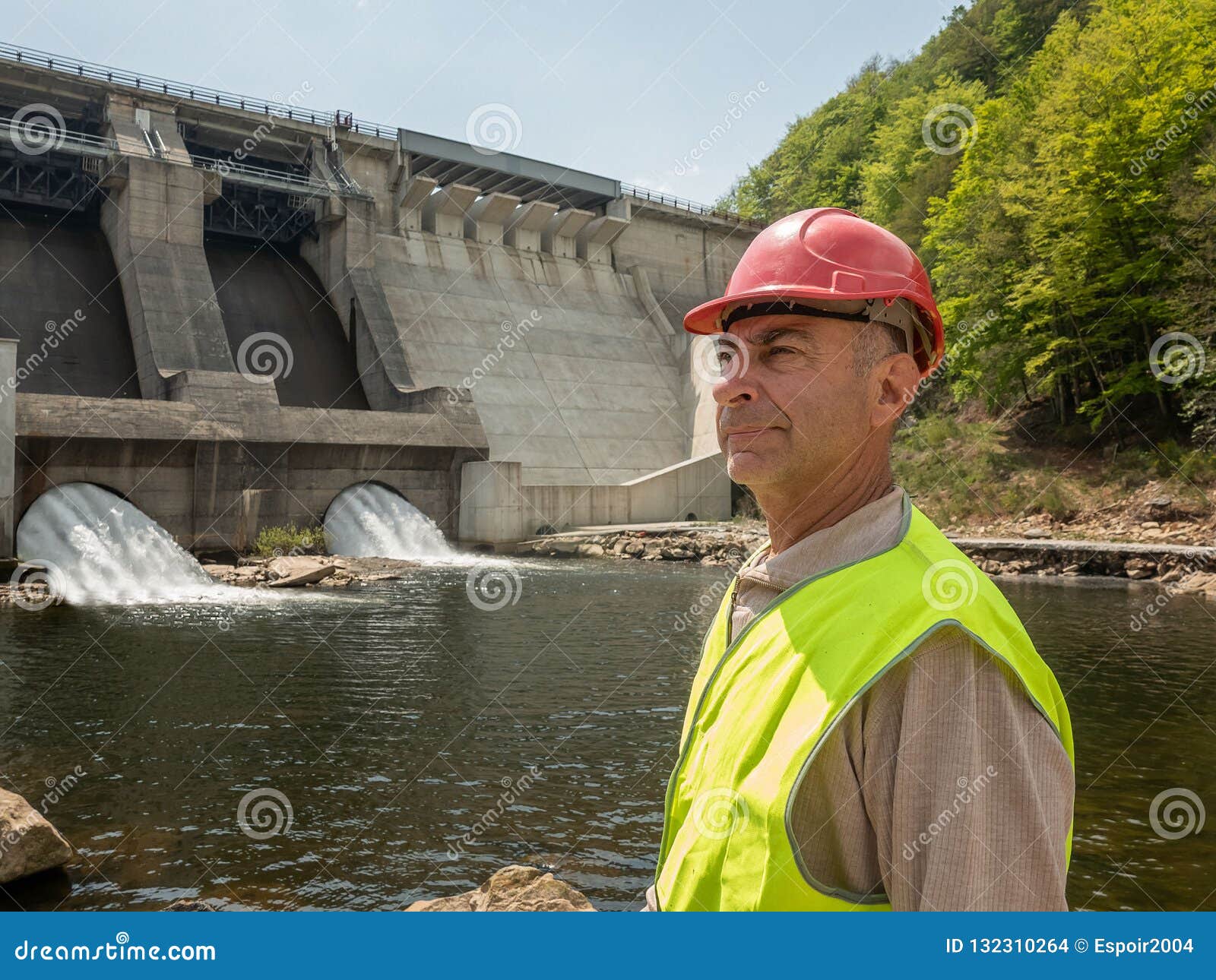 An Aging Worker in a Helmet Against the Backdrop of Hydroelectric ...