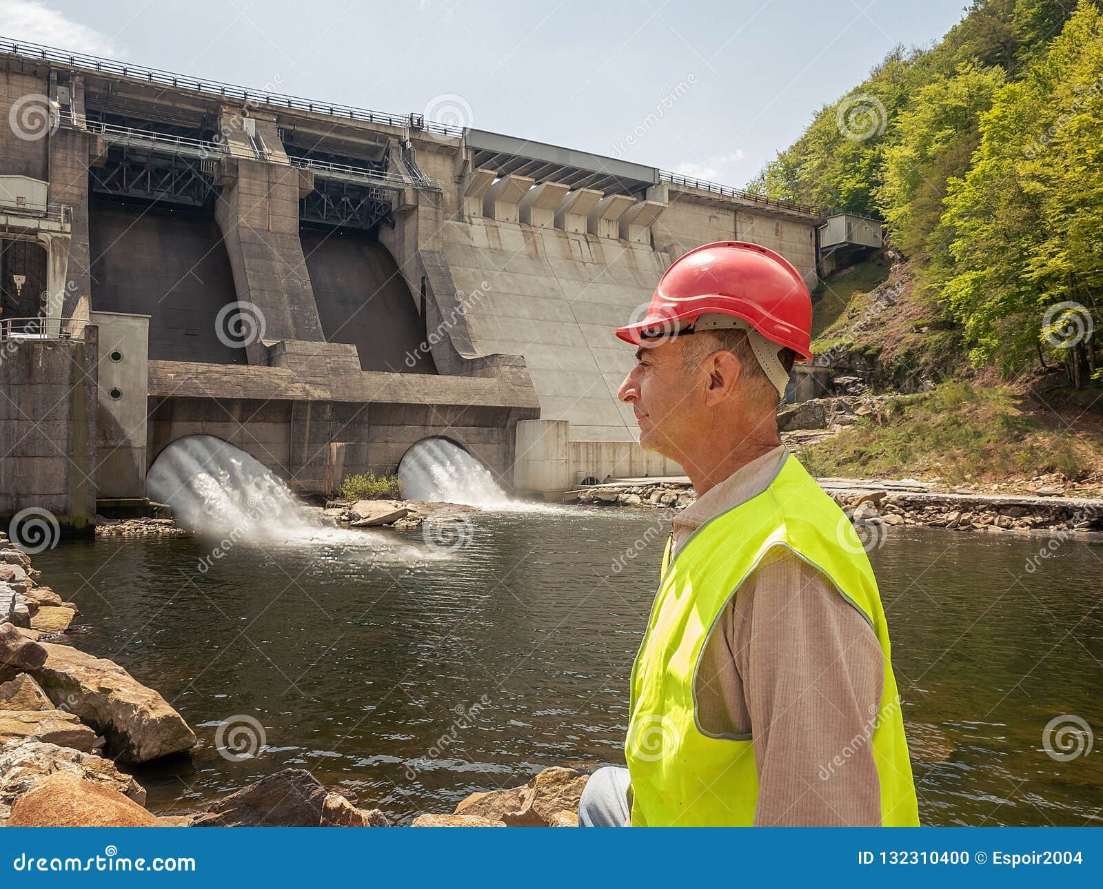 An Aging Worker in a Helmet Against the Backdrop of Hydroelectric ...
