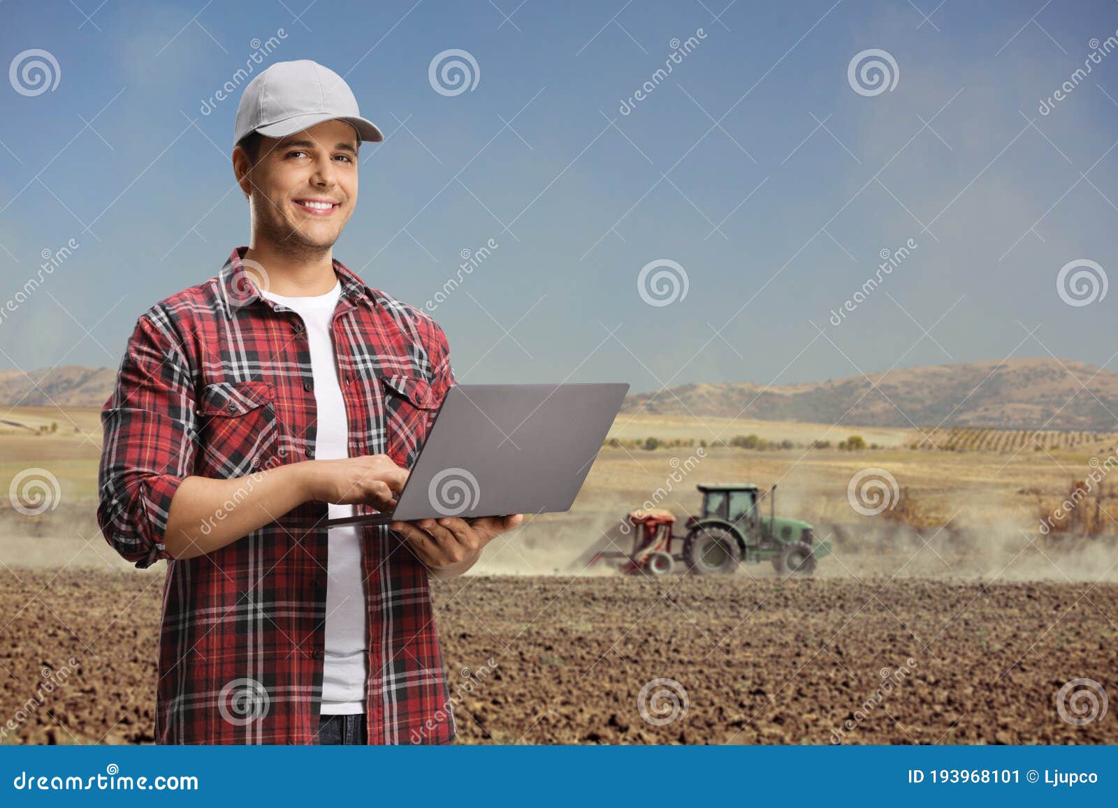 Agricultural Engineer in a Field with a Laptop and a Tractor Plowing ...