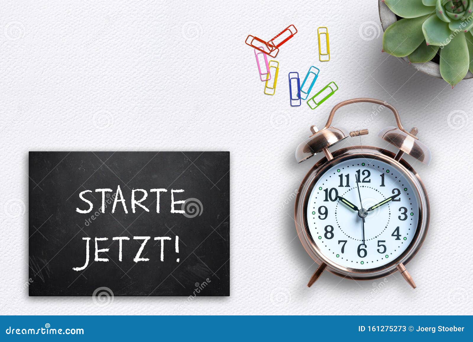 Alarm Clock Next To Slate Plate with Text `Start Now!` in German Stock ...
