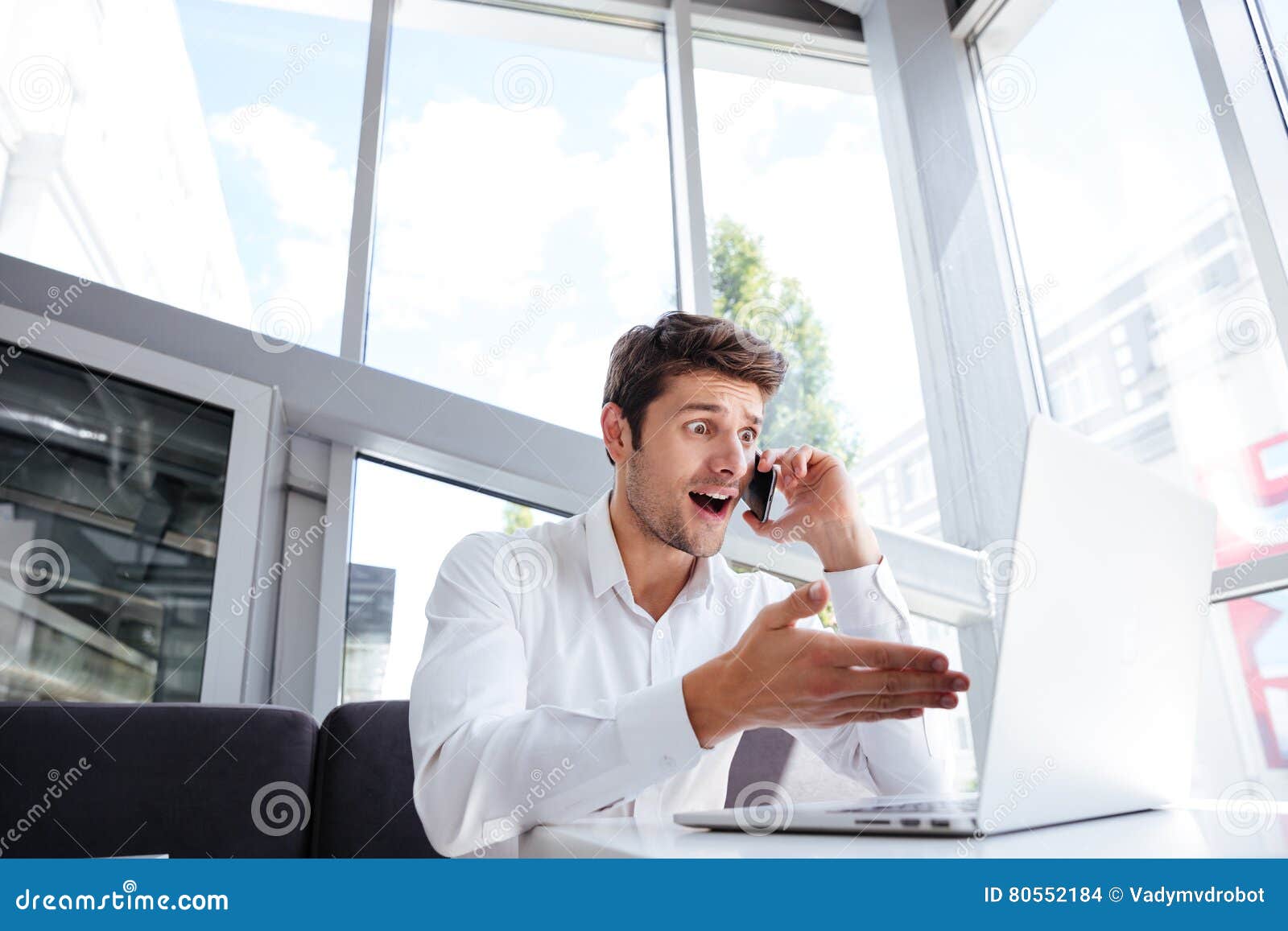 Amazed Young Businessman Using Laptop and Talking on Mobile Phone Stock ... Amazed Young Businessman Using Laptop and Talking on Mobile Phone Stock ...