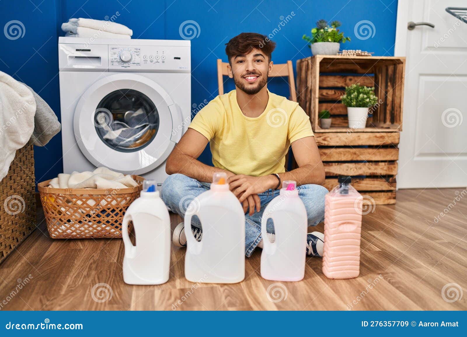 Arab Man With Beard Doing Laundry Sitting On The Floor With Detergent Bottle With A Happy And