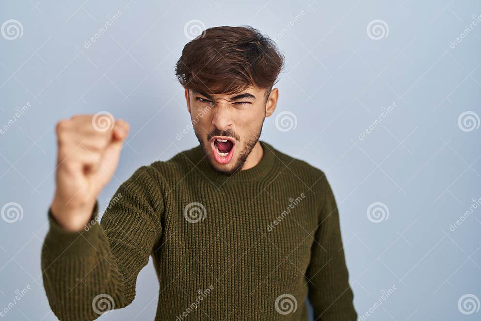 Arab Man With Beard Standing Over Blue Background Angry And Mad Raising Fist Frustrated And