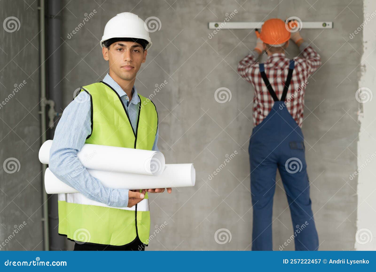 Architect Man with Blueprints and a Working Builder in the Background ...