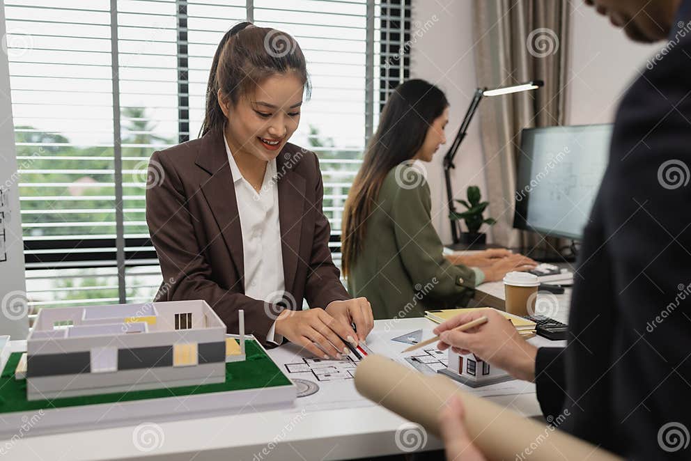 An Architect is Working in the Office with His Team, Blueprint on the Desk, Contractor Working ...
