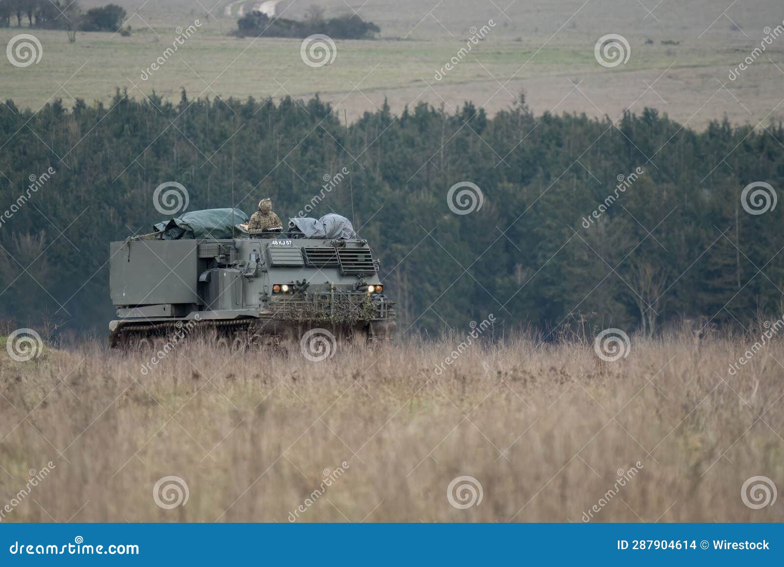 Army MLRS in Action Driving through a Large Grassy Field with Trees in ...