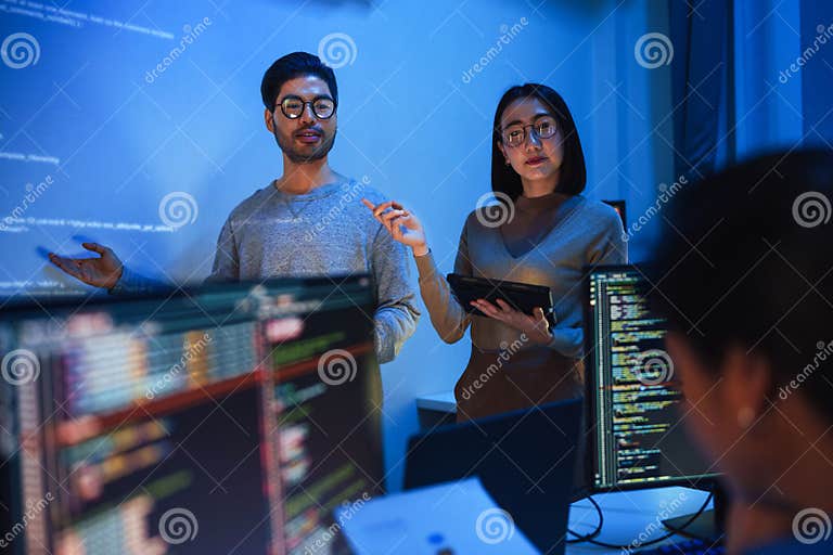 Asian Developer Leads Present Code Review Session, Pointing at Code Projected on the Wall with ...