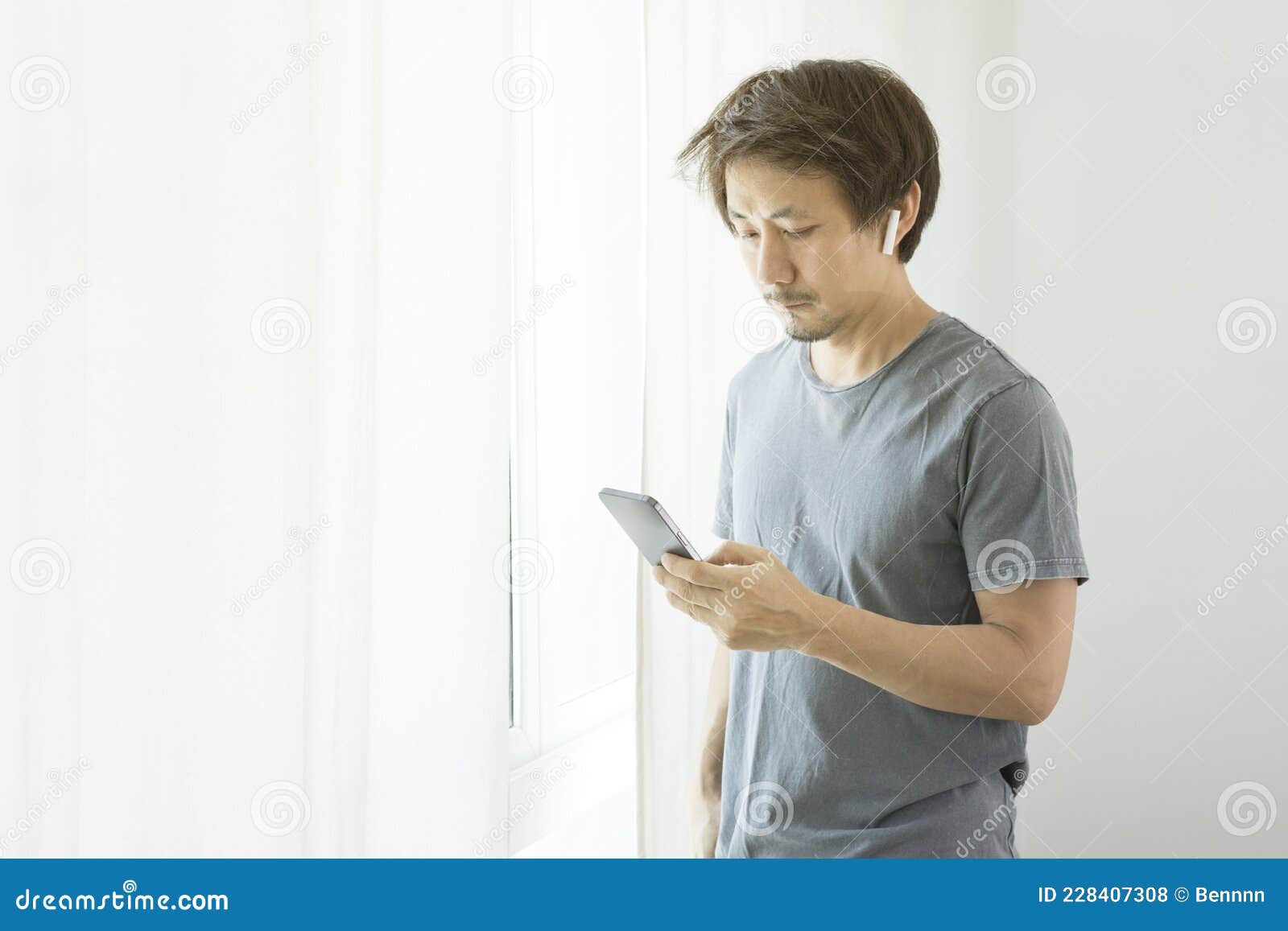 Asian Guy Using Voice Assistant on Cellphone with Earpod by the Window ...