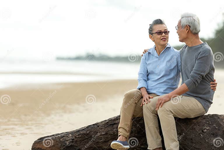 Asian Lifestyle Senior Couple Hug And Sitting On The Beach Happy In