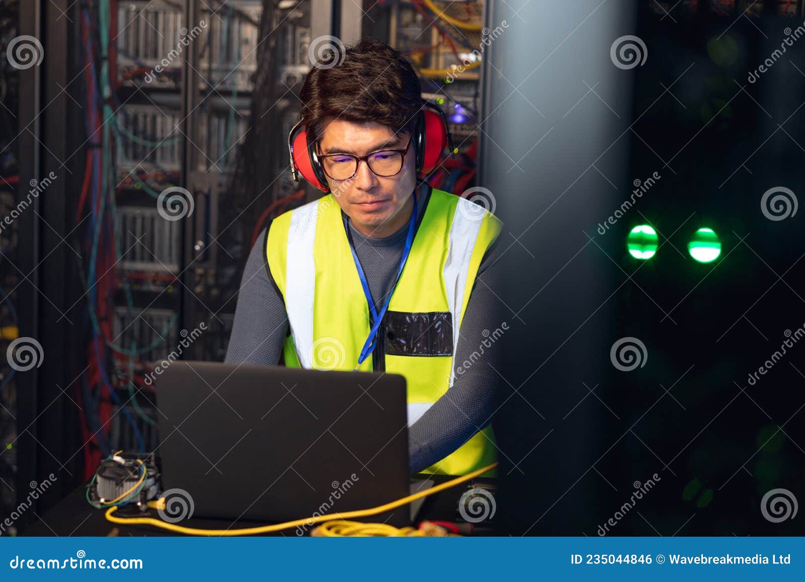 Asian Male Engineer Wearing Ear Plugs Using a Laptop in Computer Server ...