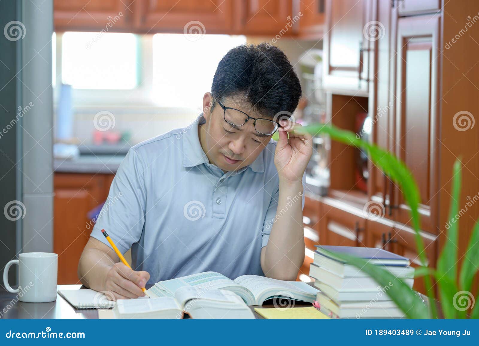 Asian Middle-aged Man Sitting At Desk At Home, Reading A Book And ...
