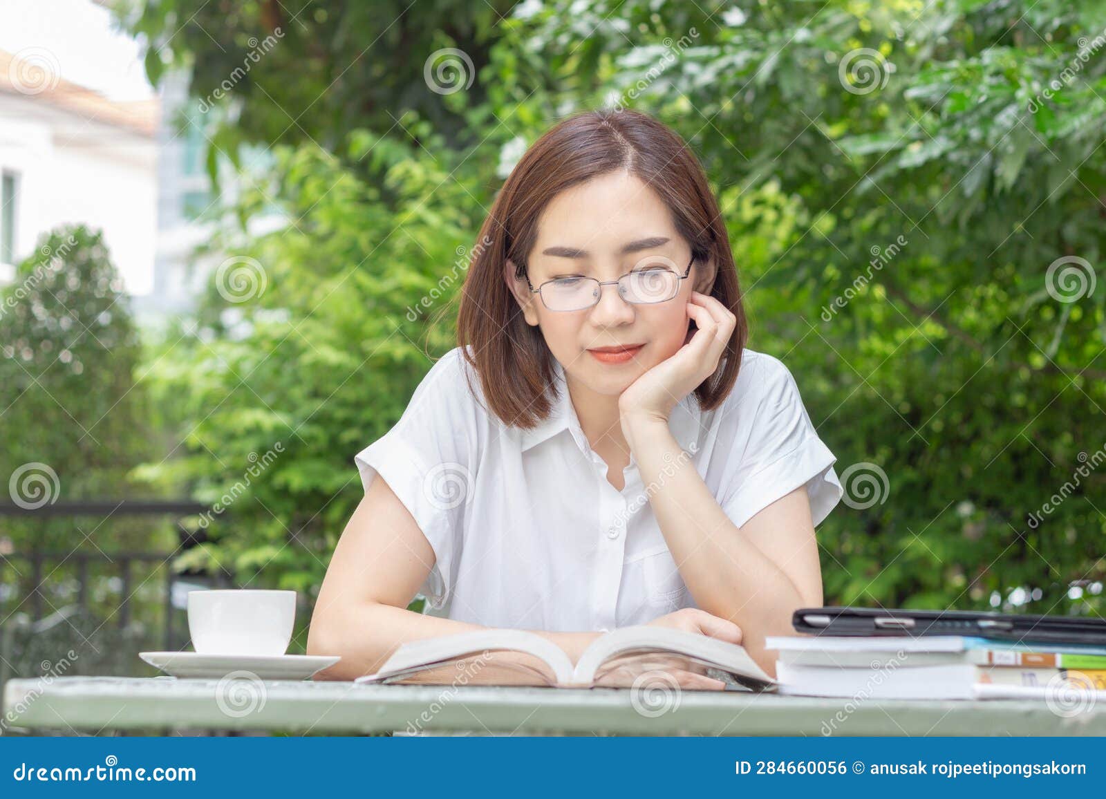 Asian Middle Aged Woman In Glasses Reading A Book In Backyard Stock