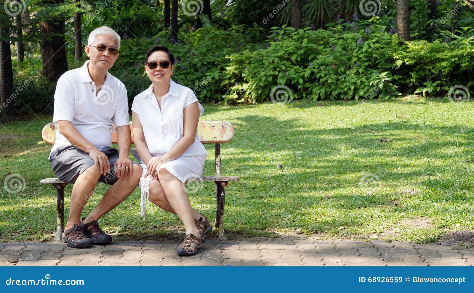 Asian Senior Couple Sitting At Bench In The Park With Copy Space Stock