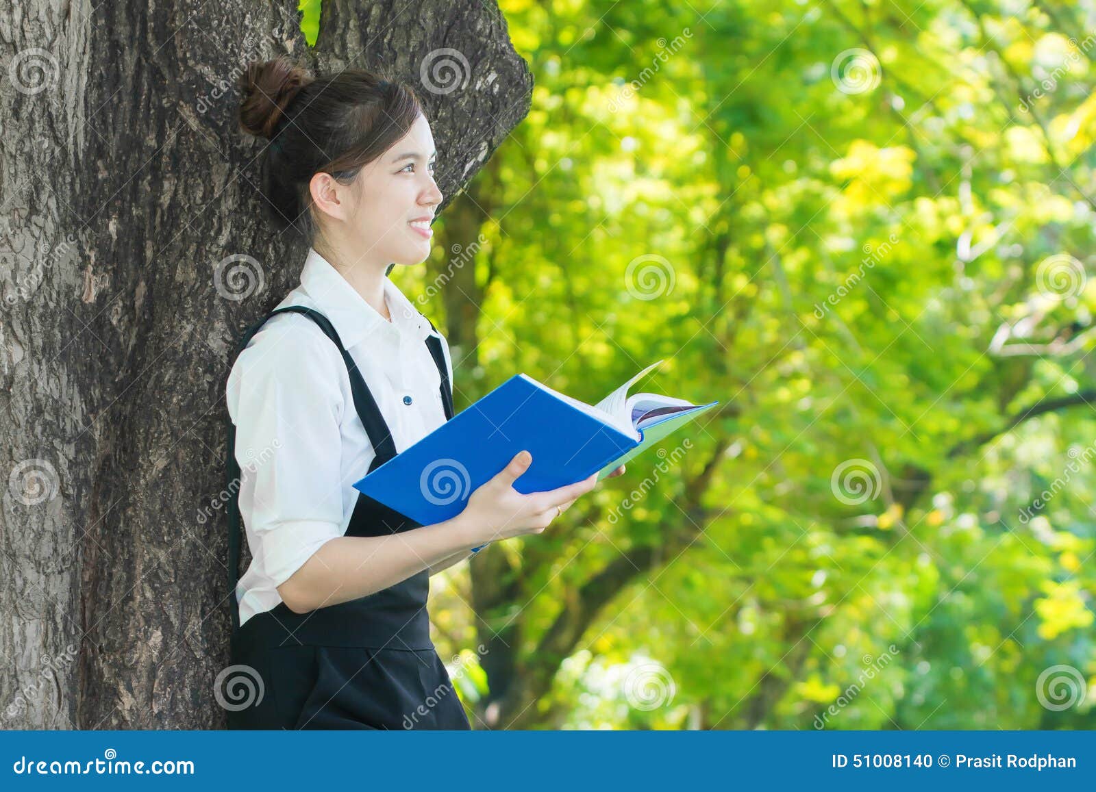 Asian Student Reading Blue Book, Against Green of Summer Park. Stock ...