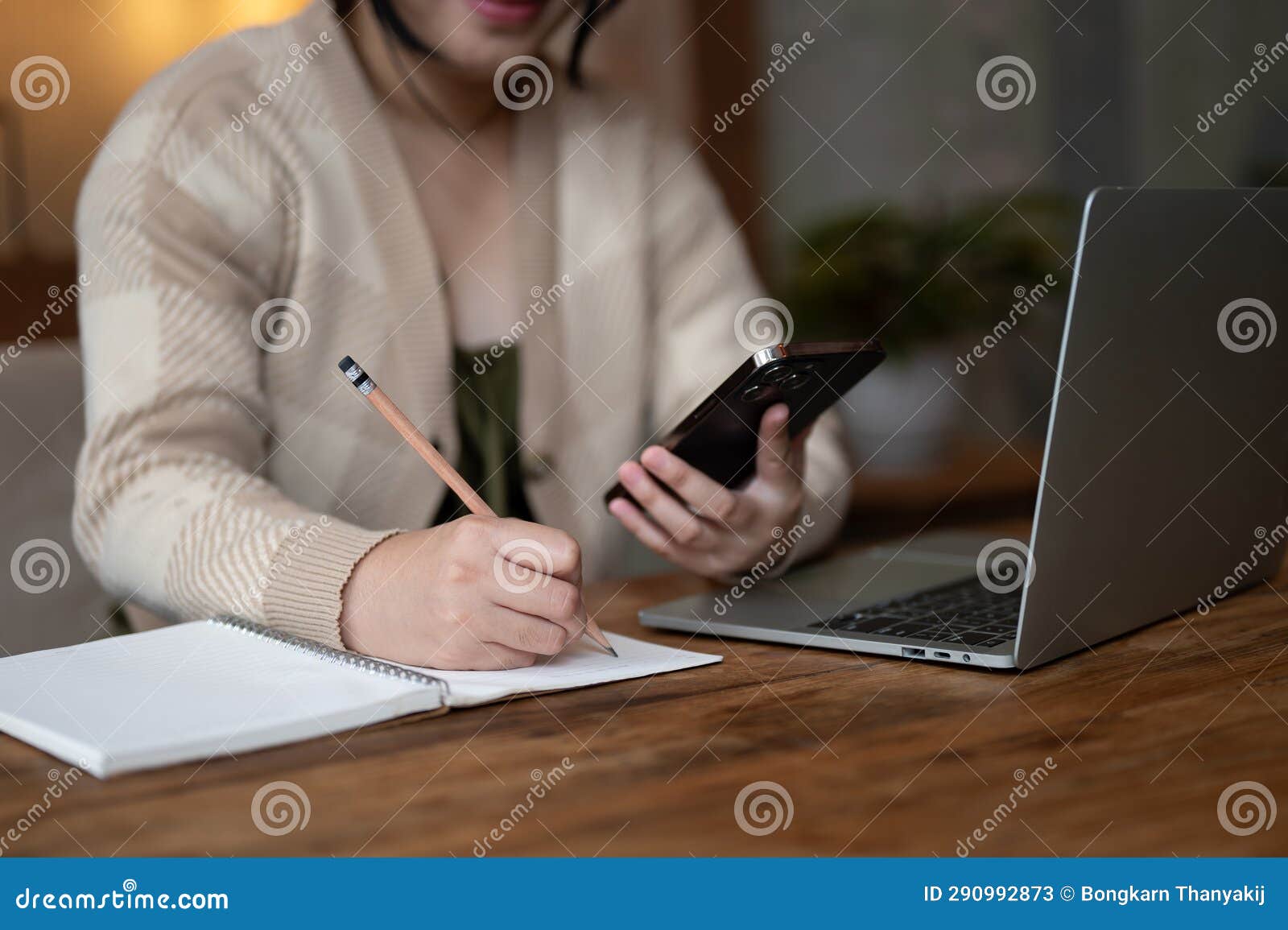 An Asian Woman Using Her Smartphone and Taking Notes on Paper while ...