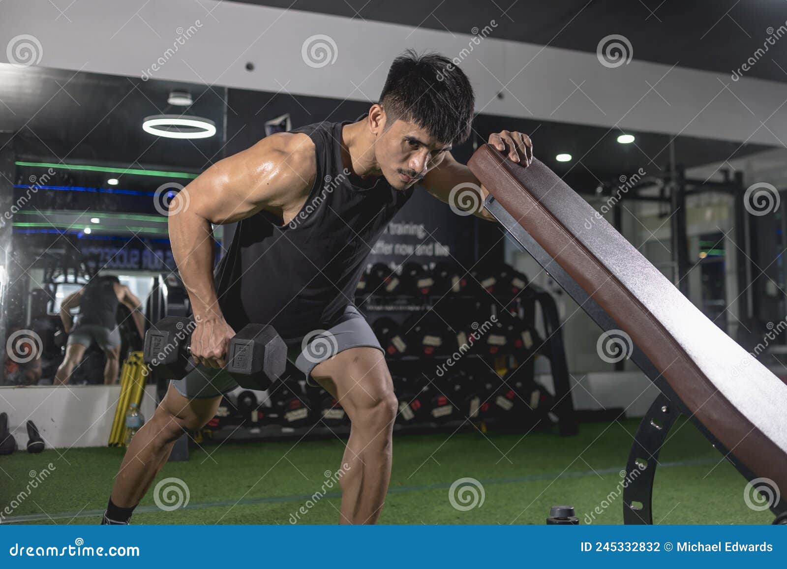 An Athletic Asian Man Does One-arm Dumbbell Rows while Leaning on an ...