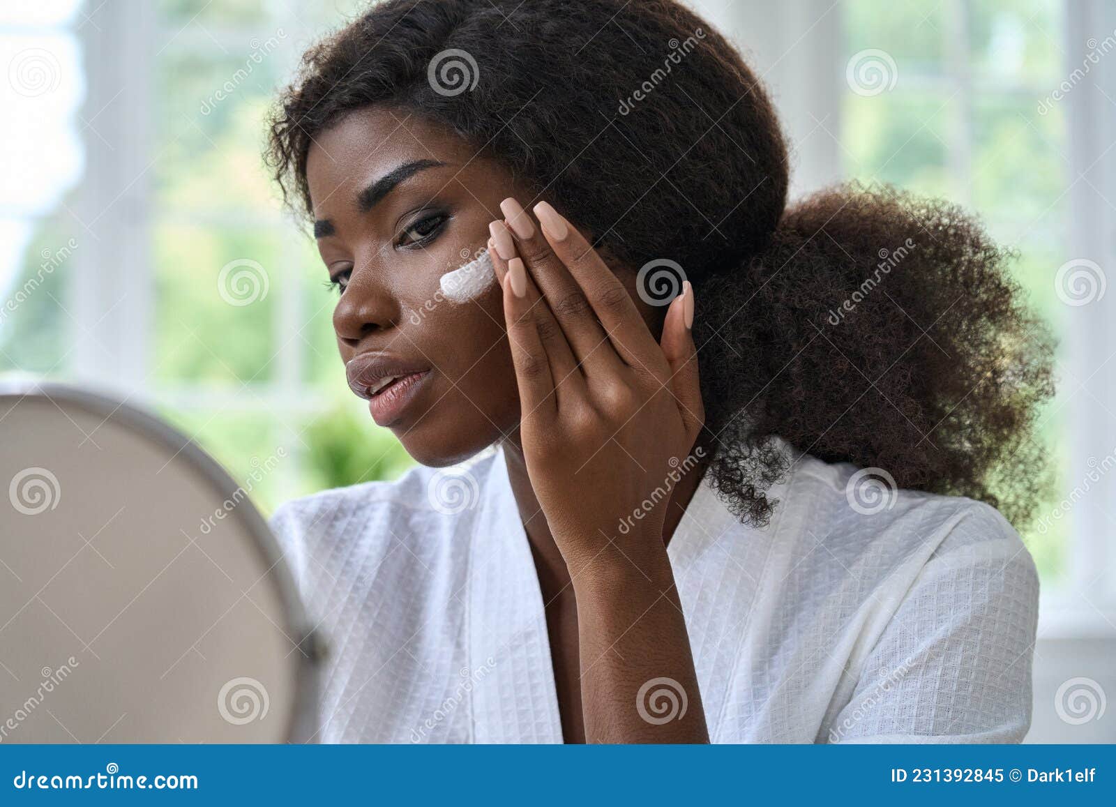 Attractive Black Young Woman Applying Cream On Face Skin Looking In