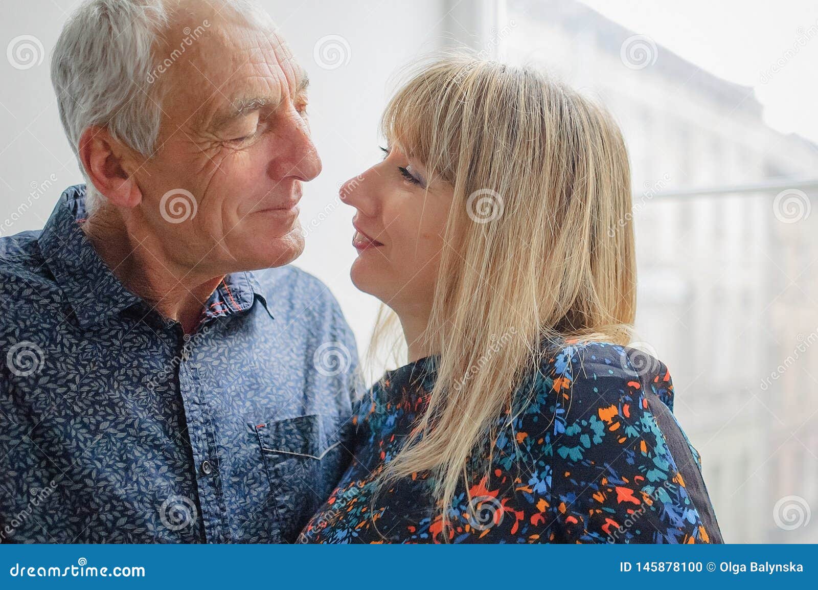 Attractive Blond Woman Hugging Handsome Senior Man And Looking At Him