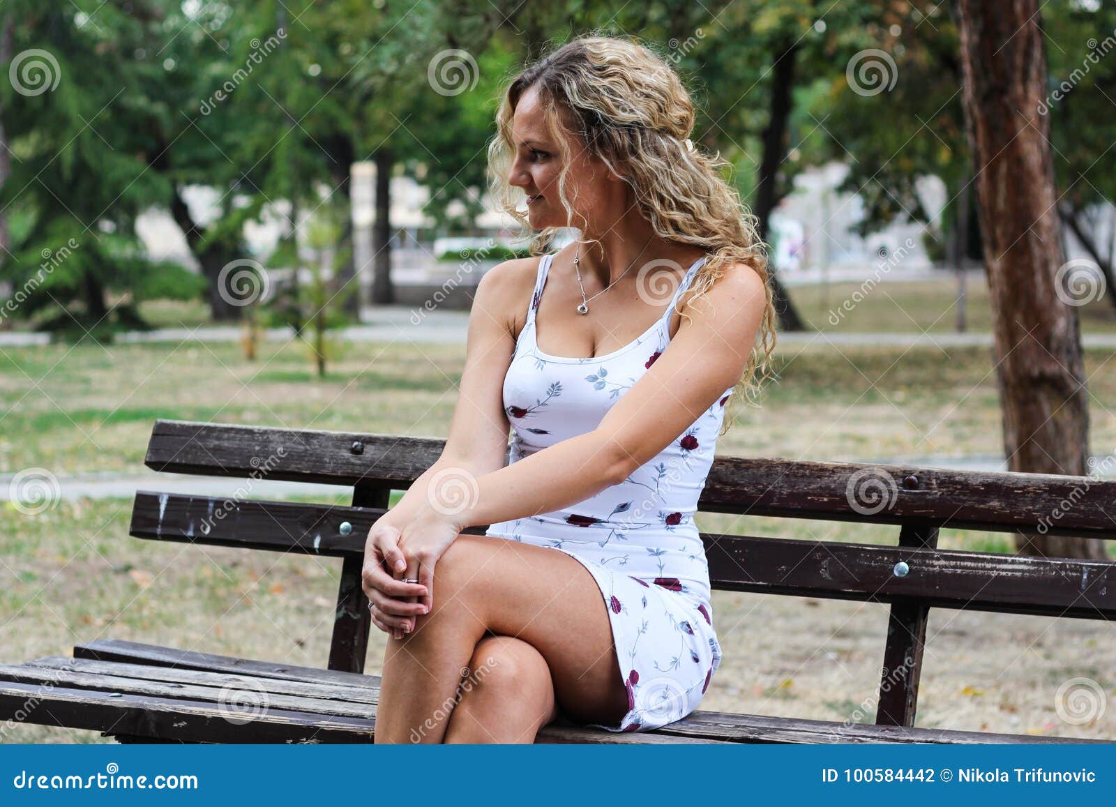 Attractive Blonde Girl With Curly Hair Sitting On The Bench In A Stock