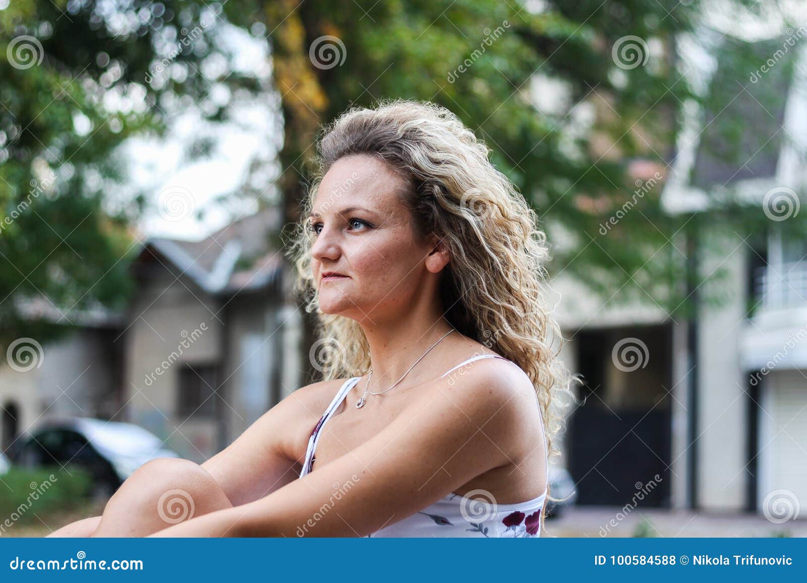 Attractive Blonde Girl With Curly Hair Sitting On The Bench In A Stock