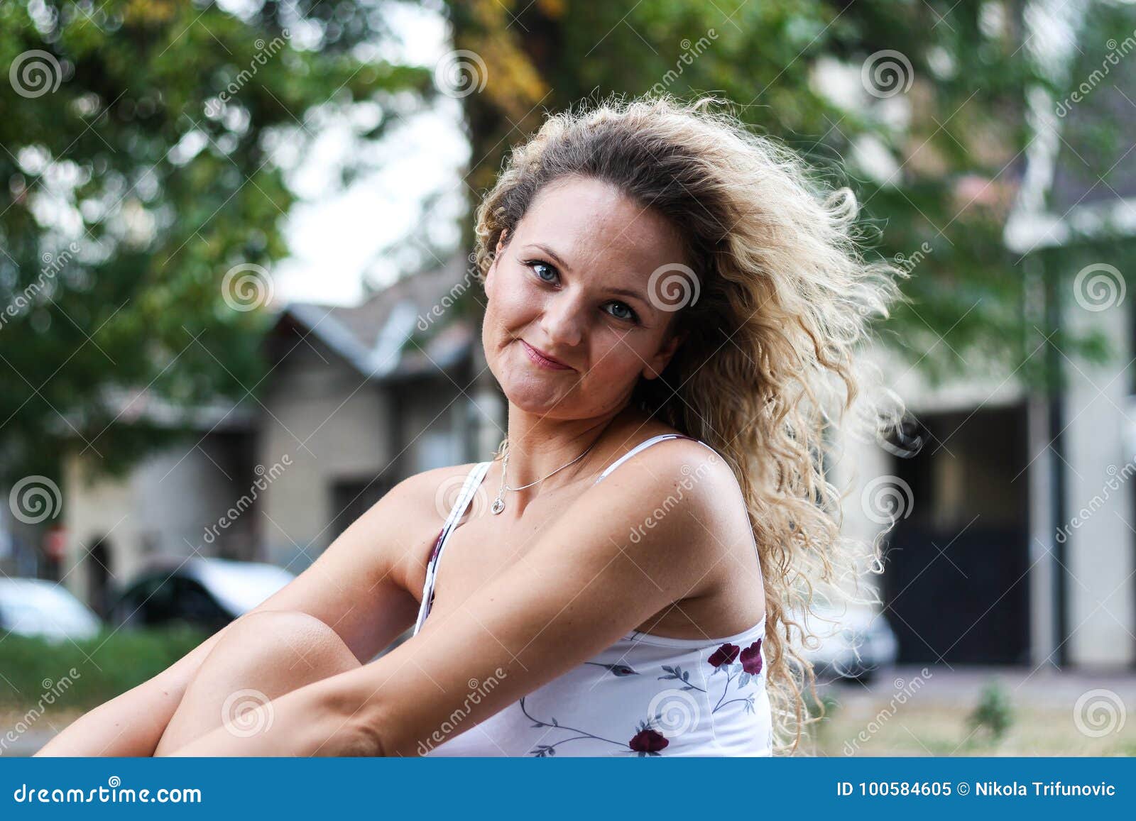 Attractive Blonde Girl With Curly Hair Sitting On The Bench In A Stock