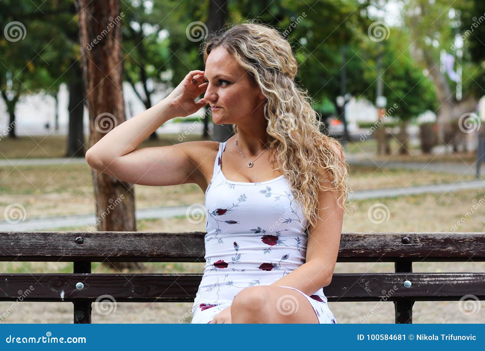 Attractive Blonde Girl With Curly Hair Sitting On The Bench In A Stock