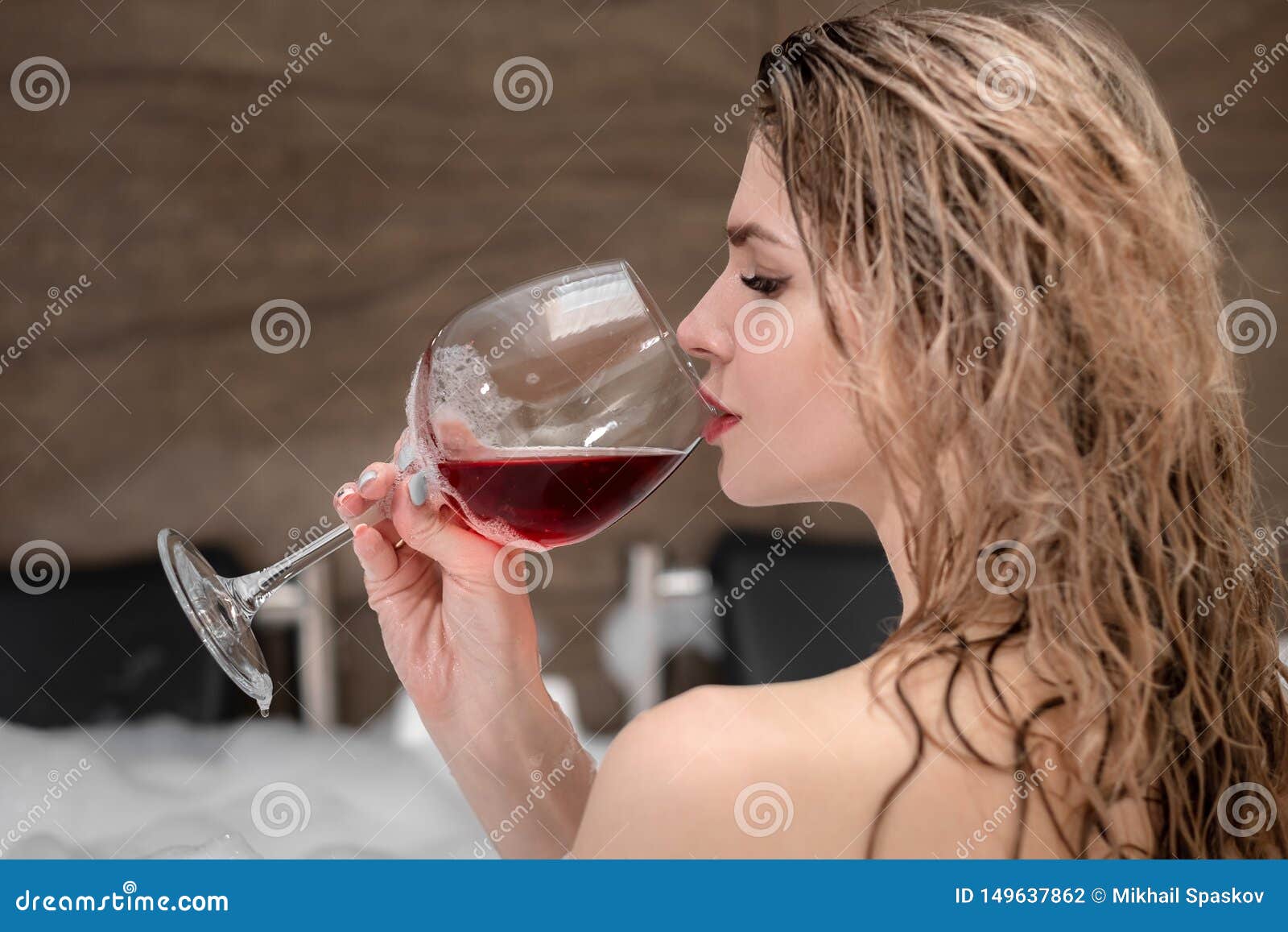 Attractive Blonde Woman Lying In Bathtub In Foam In Hotel Drinking Red