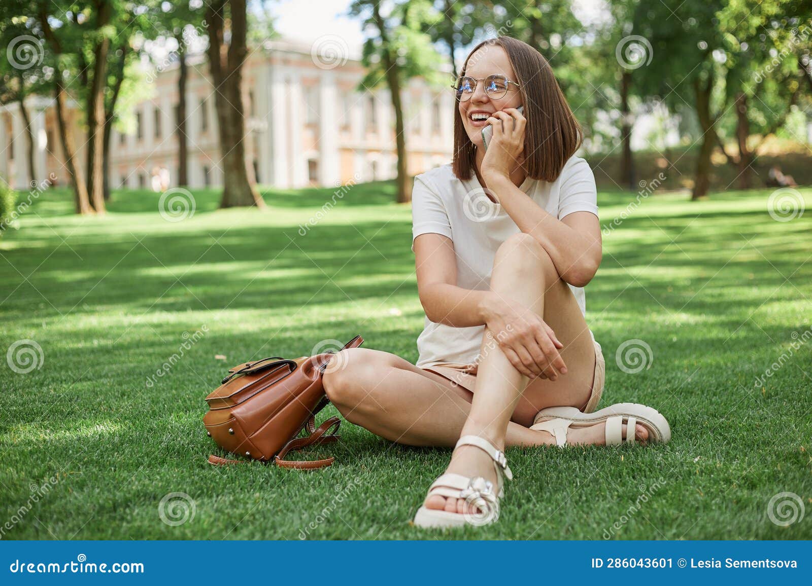 Attractive Cheerful Woman Wearing White T Shirt Sitting On Grass In