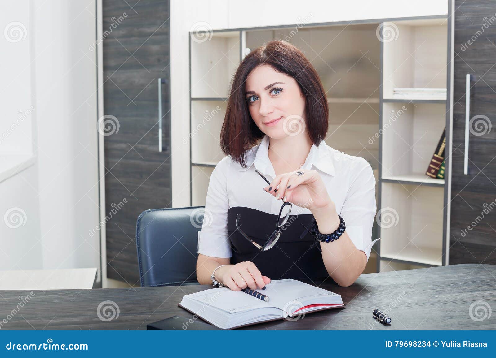Attractive Dark Haired Woman Wearing A Black And White Blouse Sitting
